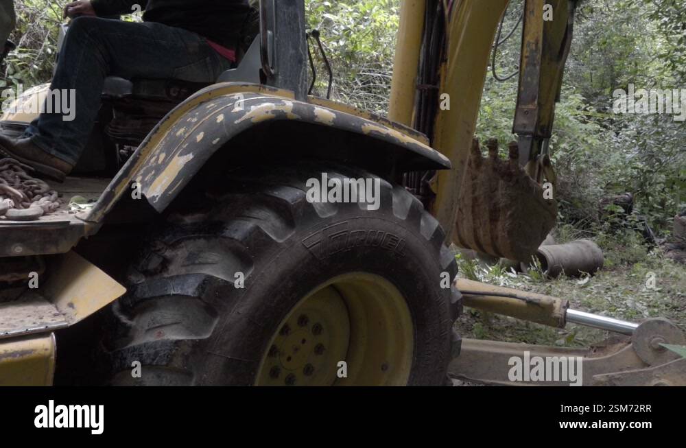 A backhoe loader parking and lowering its stabilizers in the forest ...