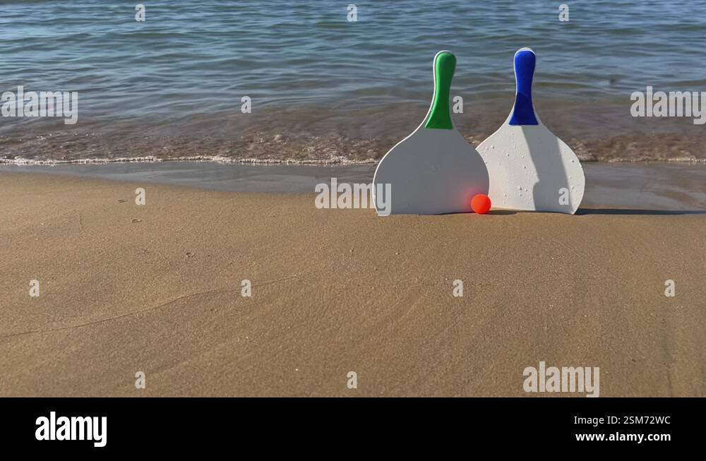 Beach tennis paddle rackets and red balls on sandy beach with waves ...