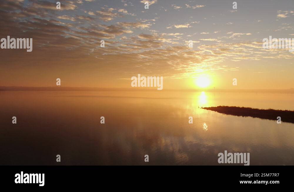 Sun rises and reflects bouncing off of misty lake with dramatic sky ...