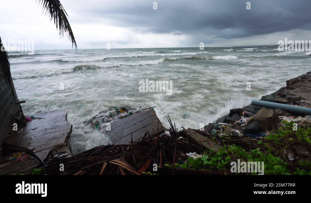 Tilt up shot showing crashing waves of ocean reaching polluted beach ...
