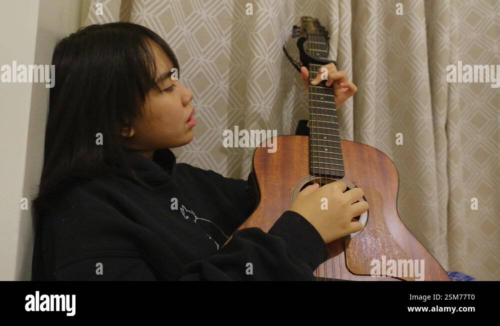 Attractive filipino girl strumming acoustic guitar and jamming. Static ...