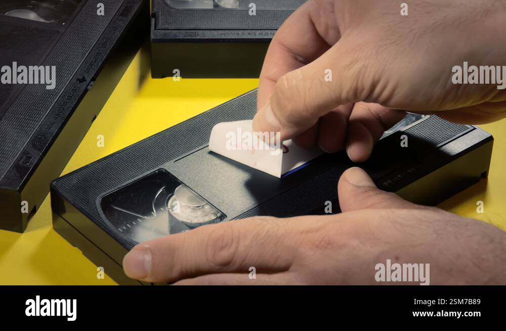 A hand applies a handwritten label to a VHS tape, with the text 1980s ...