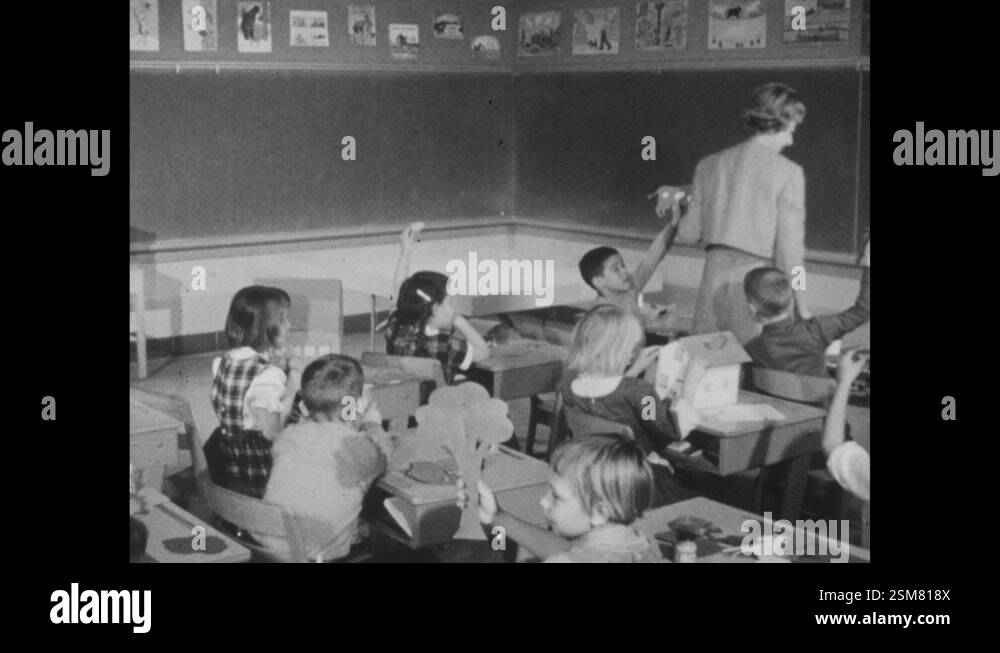 1960s: Teacher in a classroom of children, holding up paper farm shapes ...