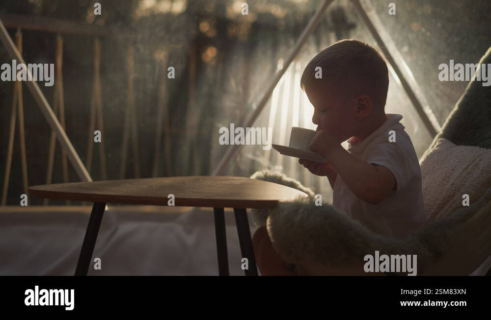 Child takes sip of tea at low table at glamping Stock Video Footage - Alamy