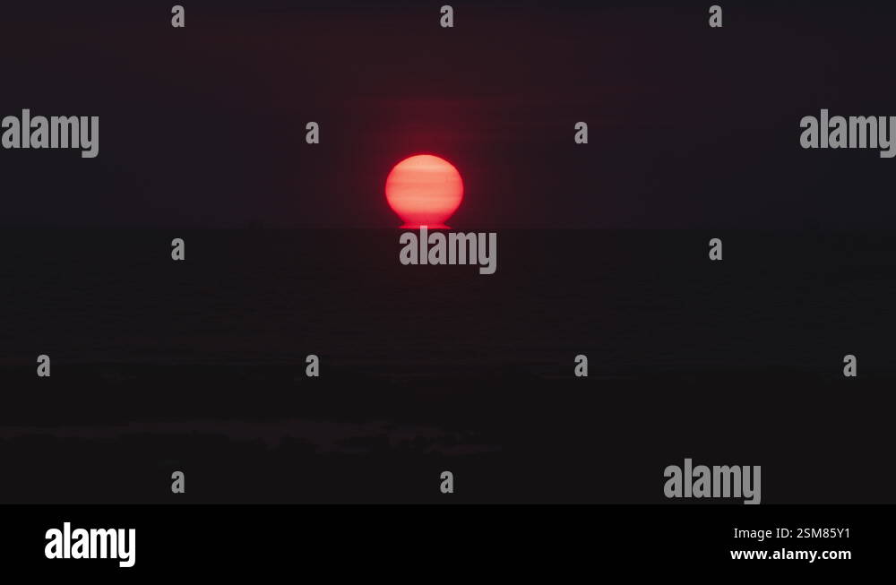 Glowing red sun sinking beyond ocean horizon in total darkness Stock ...