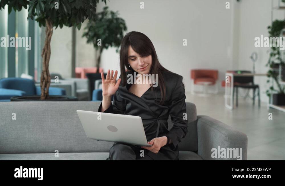 young, beautiful woman in a suit gestures goodbye, greets, and gives a ...