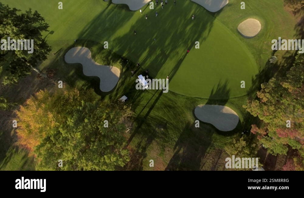 Aerial Backward Tilt Up Shot Of People Playing Golf On Course By Trees ...
