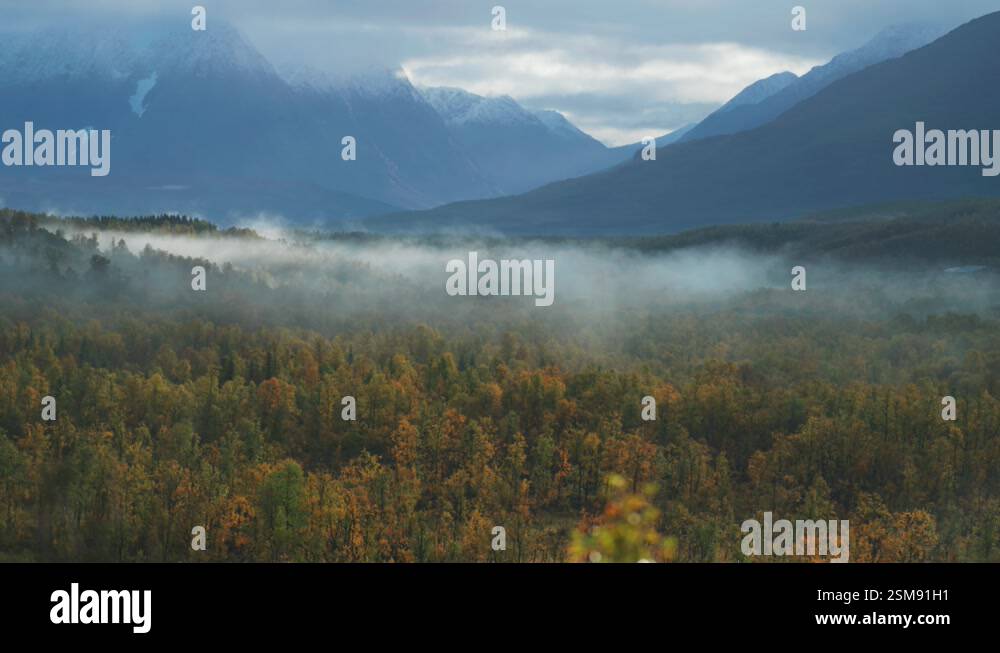 Thin fog creeps above the mountainous valley as the sun rises and lits ...