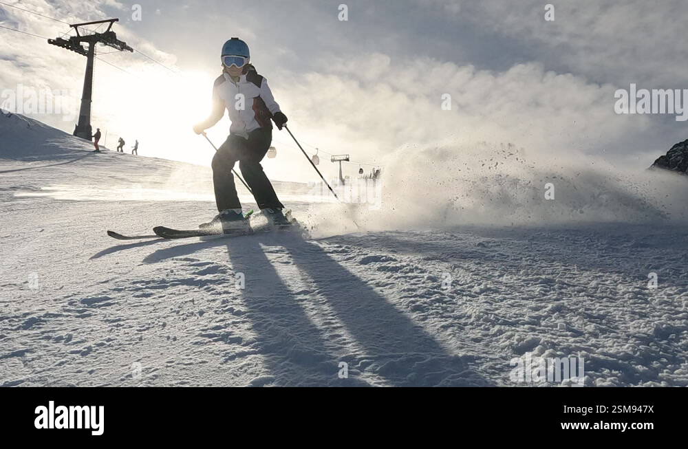LENS FLARE, SLOW MOTION: Female skier carving and spraying snow towards ...