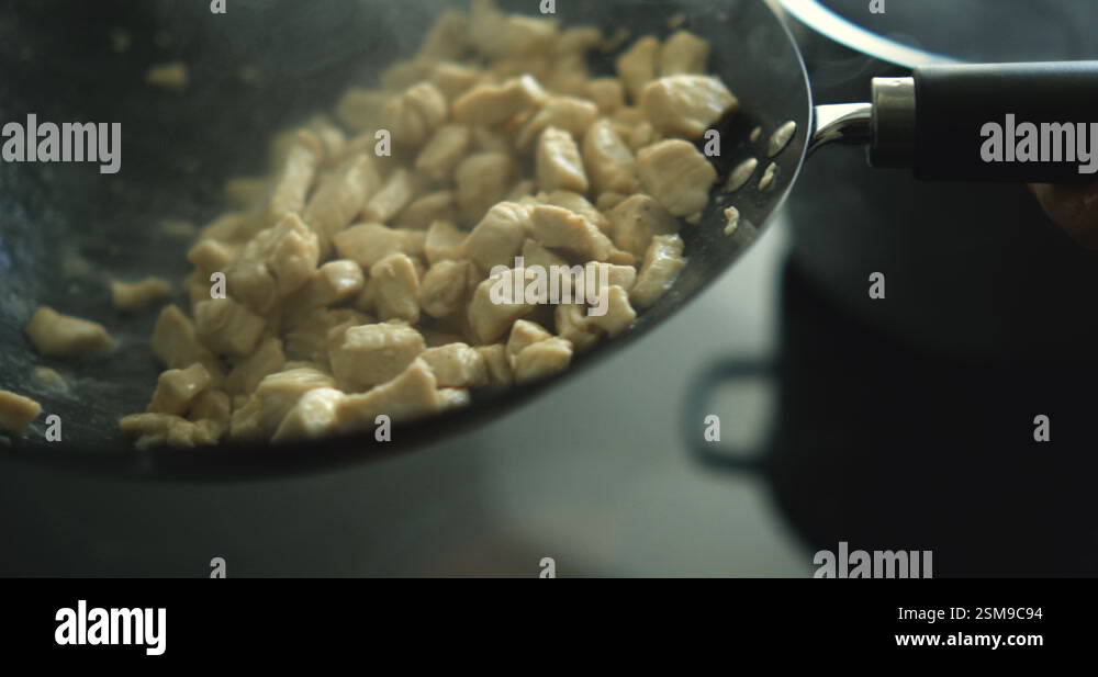 Tossing and stirring chicken pieces inside hot pan, food preparation at ...