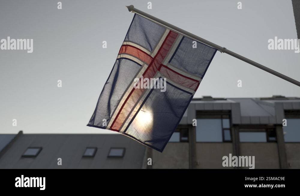 Icelandic flag waving in the wind, with buildings behind it, in slow ...