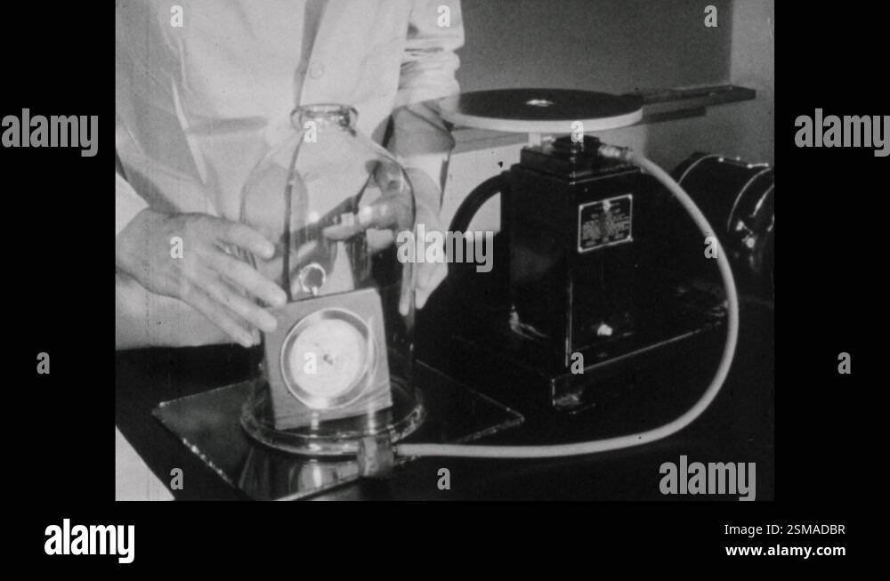 1960s: Lab. Man puts glass jar over barometer. Man attaches tube to jar ...