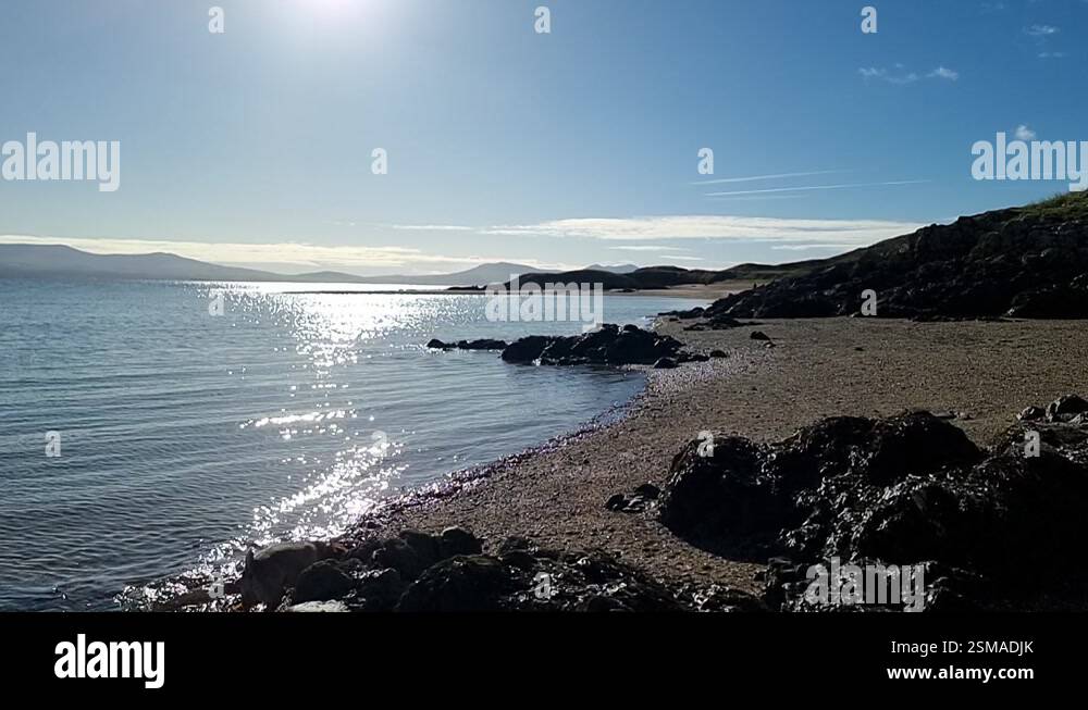 Slow pan across rocky Anglesey coastline with sunrise shimmering ocean ...