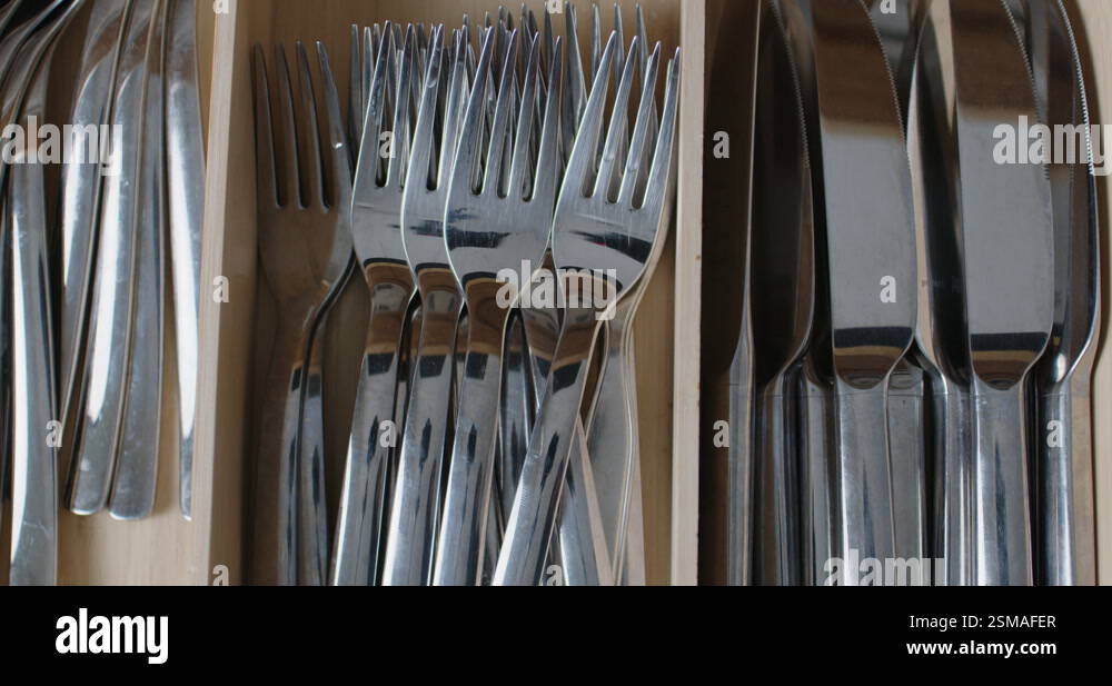 Top shot of an open kitchen drawer, putting two forks into the drawer ...