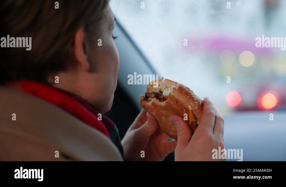 Famished woman takes bite of burger to quell hunger sitting in vehicle ...