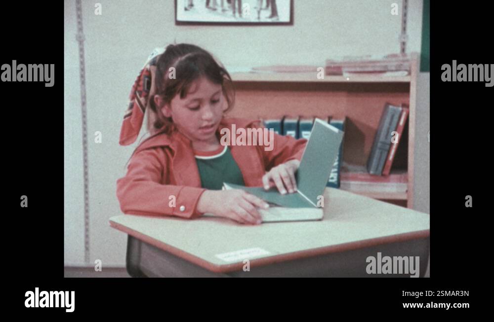 1970s: girl at classroom desk opens book with covers flat and pages ...