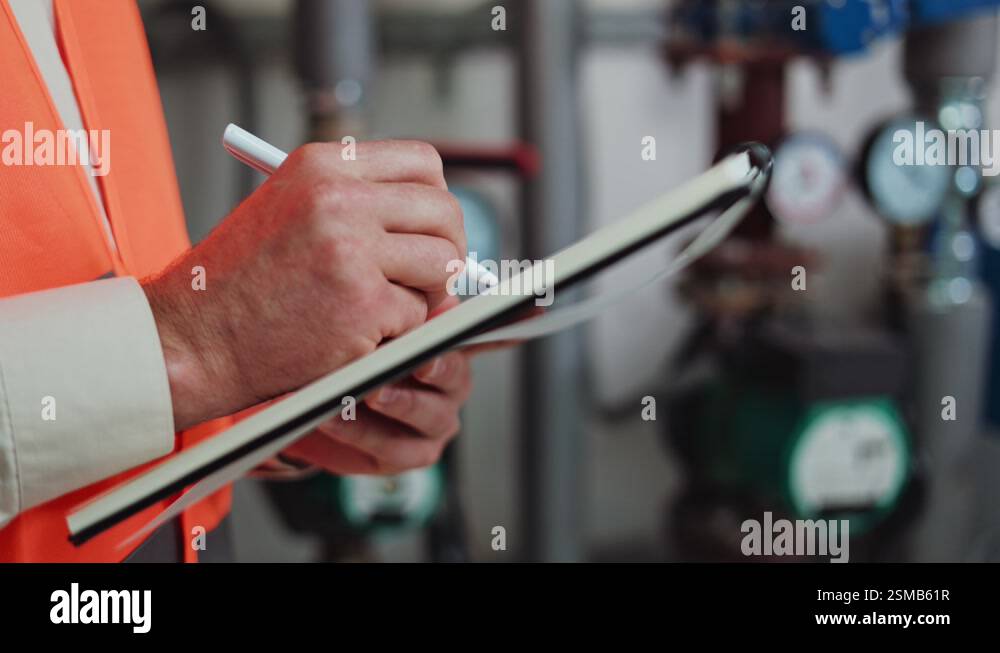 Mechanic making notes in own notebook while standing near pipes at ...