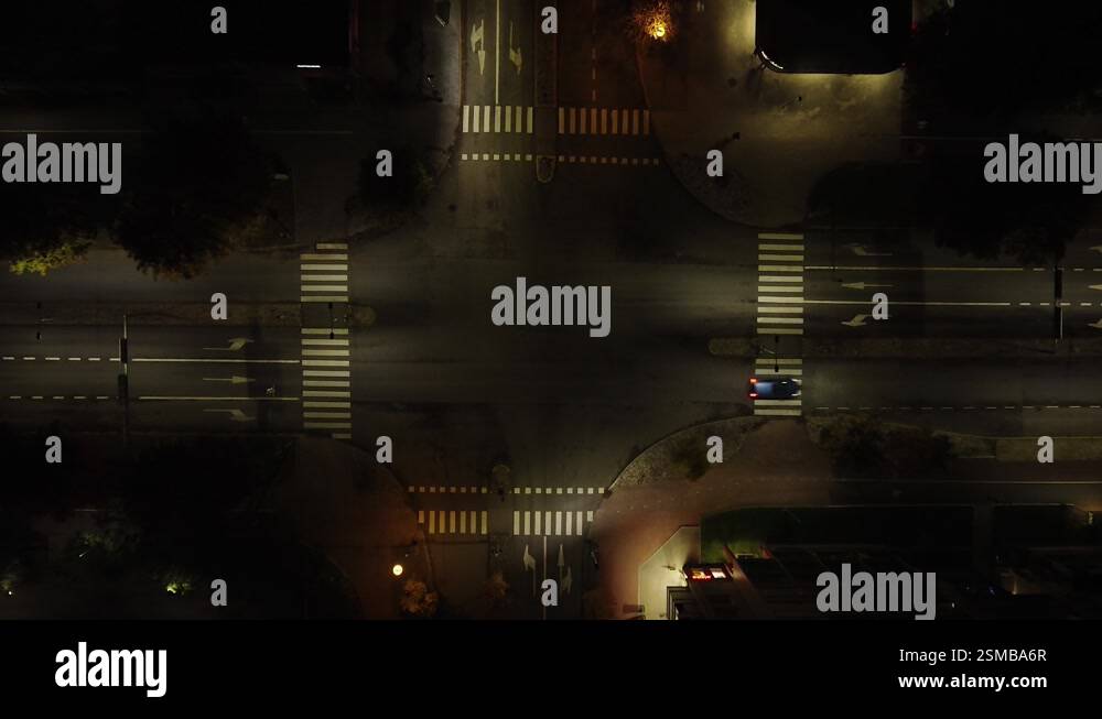 Dark night aerial descends to single blue car in city intersection ...