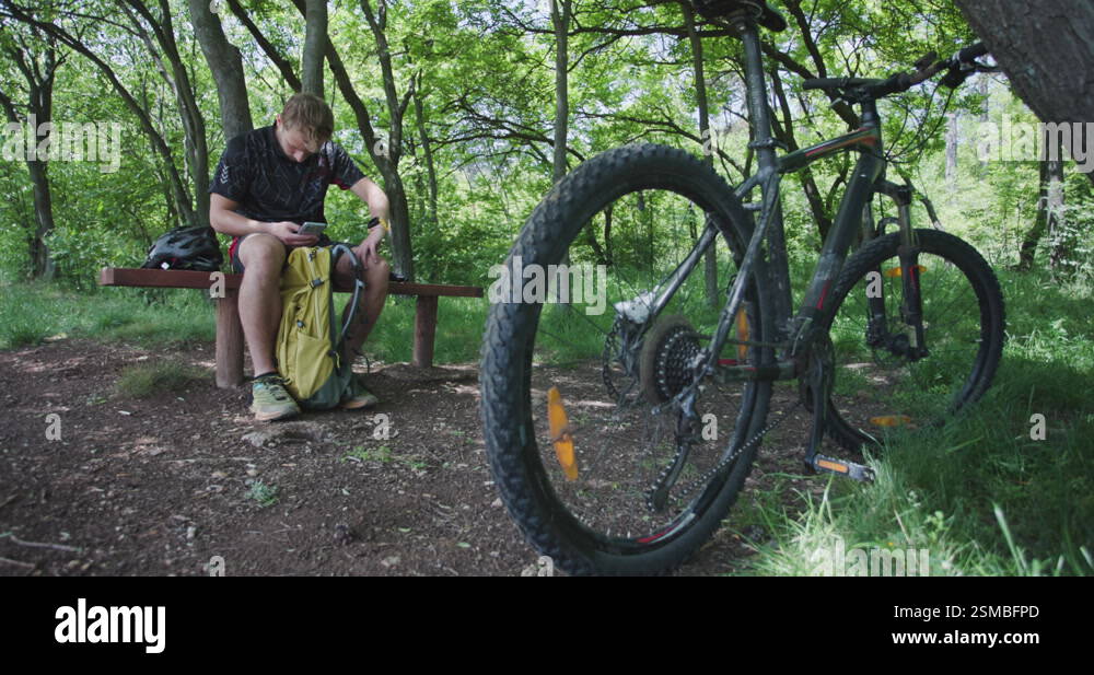 Mountain biker sitting on a bench in the forest next to his ...