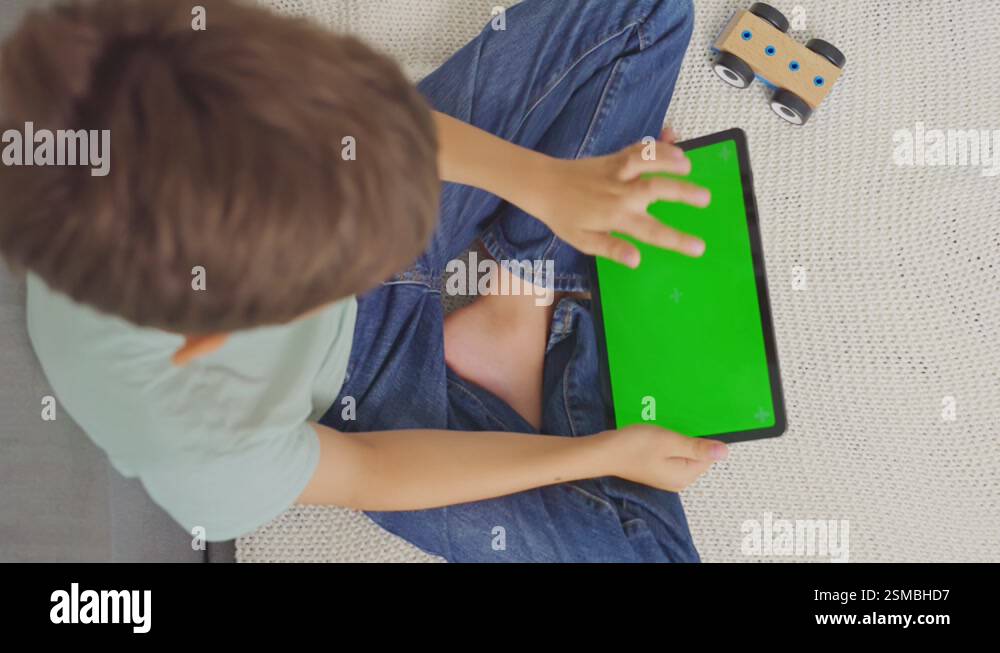 Close up kid sitting on sofa, tapping on a tablet with green screen ...