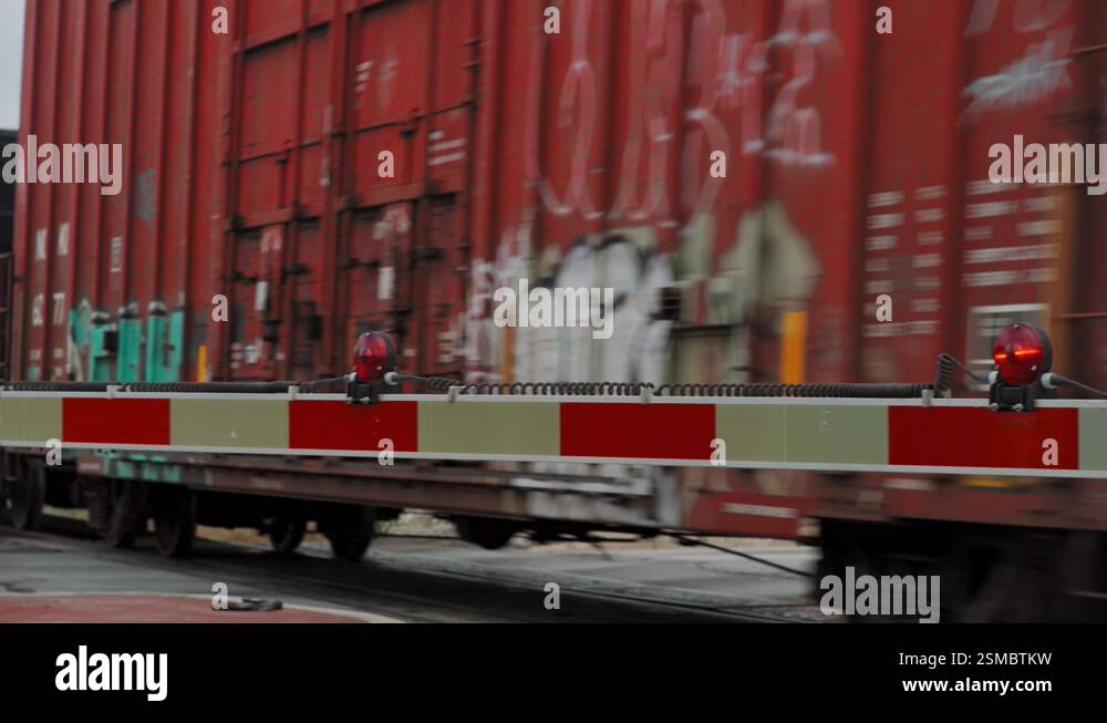 Cargo train running on level crossing with low barriers and red lights ...