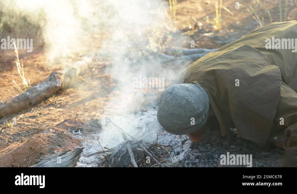 A bushman blows on a campfire to get it started in the Australian ...