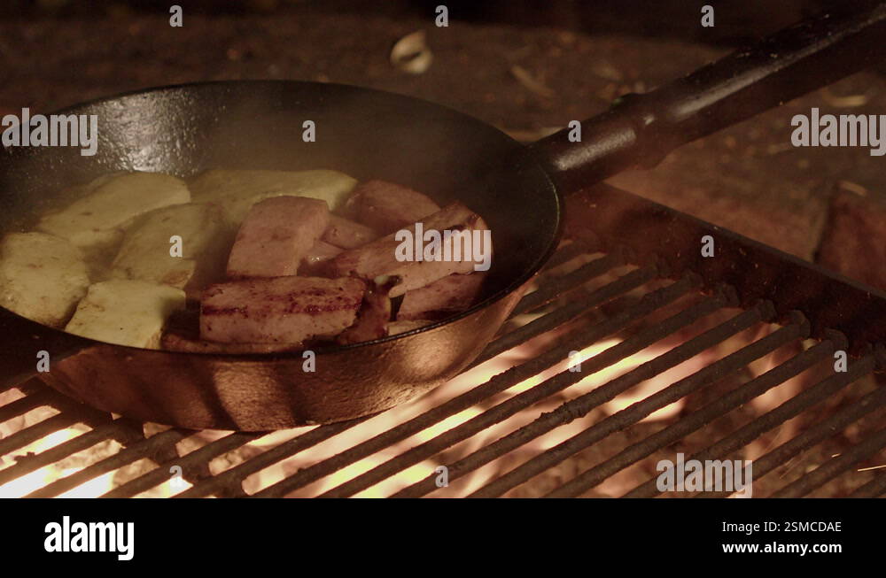 Ham and cheese slices cook in cast iron frying pan on open camp fire ...
