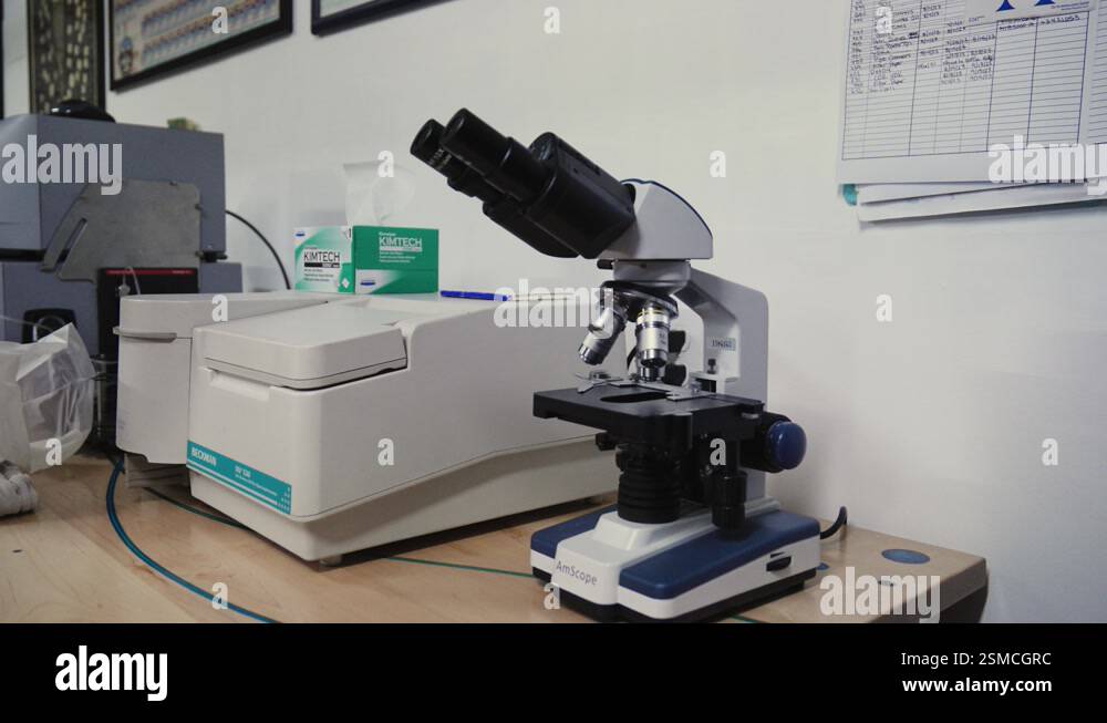 A scientist in a lab pulls a microscope from storage, removes its Stock ...