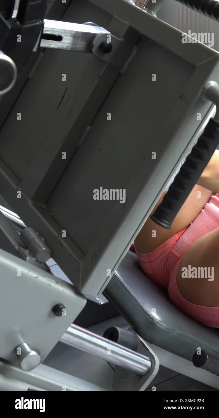 A woman performs leg exercises with weights on an exercise machine in ...