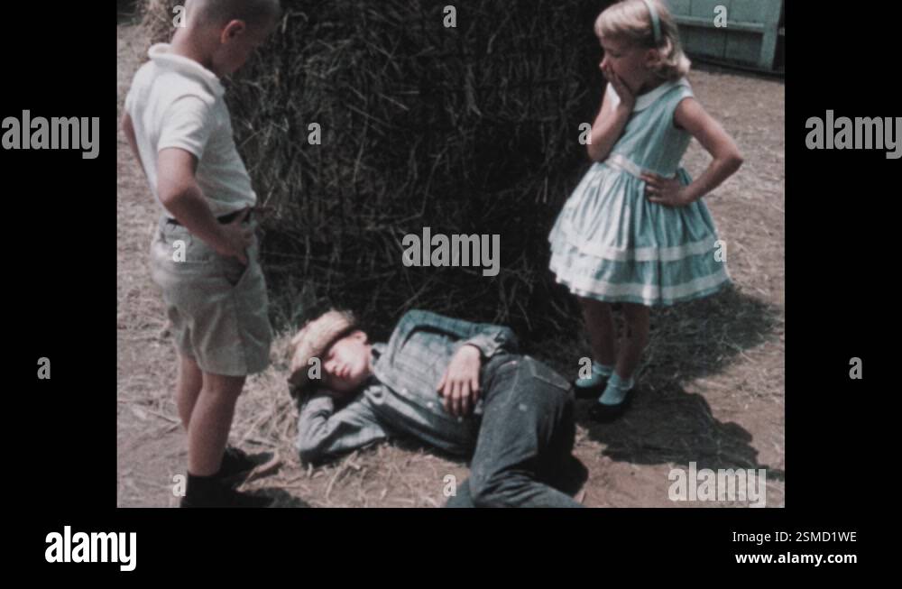 1960s: Children find little boy sleeping behind haystack. Girl puts ...