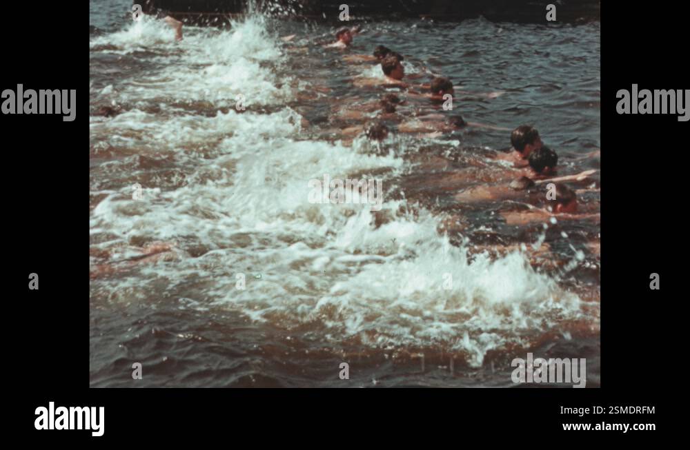 1960s: Boys in water swim toward pier. Boys jump fro pier, swim with ...