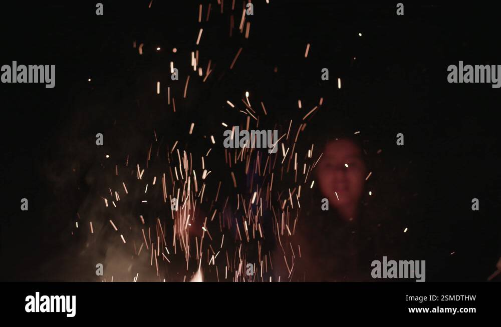 Girl looking at sparks and fire coming up from the campfire in slow ...