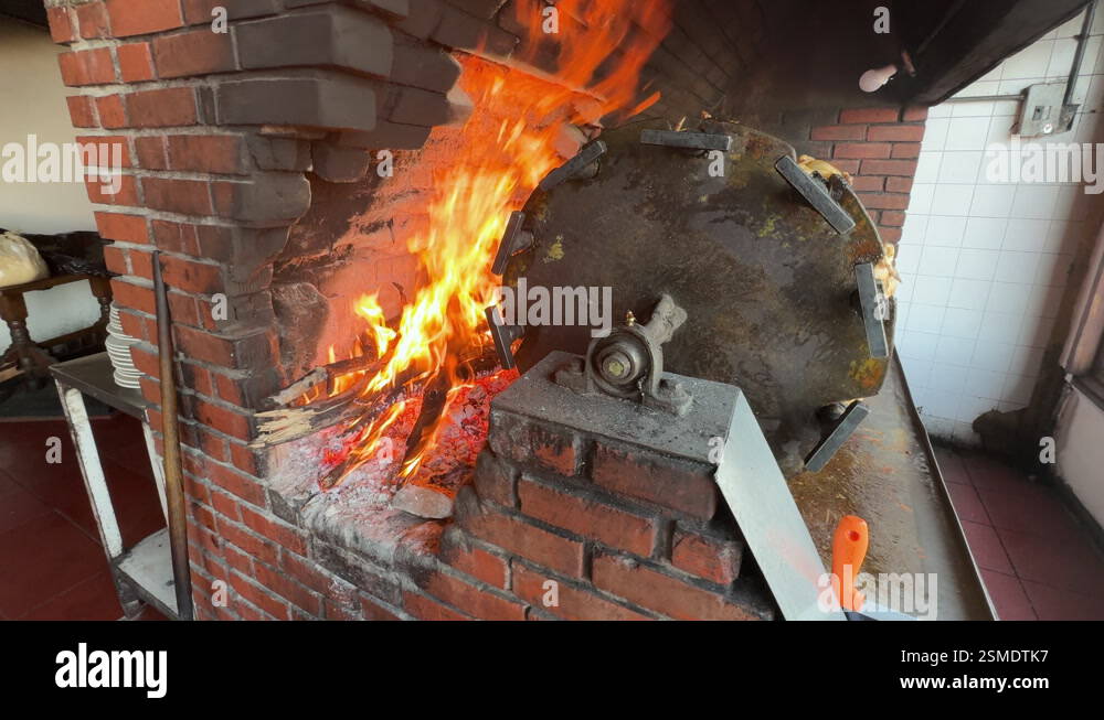 Chickens roasting on rotating spit in an open wood-fired brick oven in ...