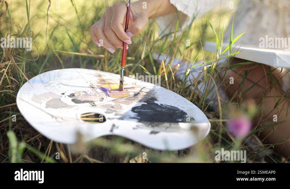 A woman artist paints a picture in nature, she uses acrylic paints ...