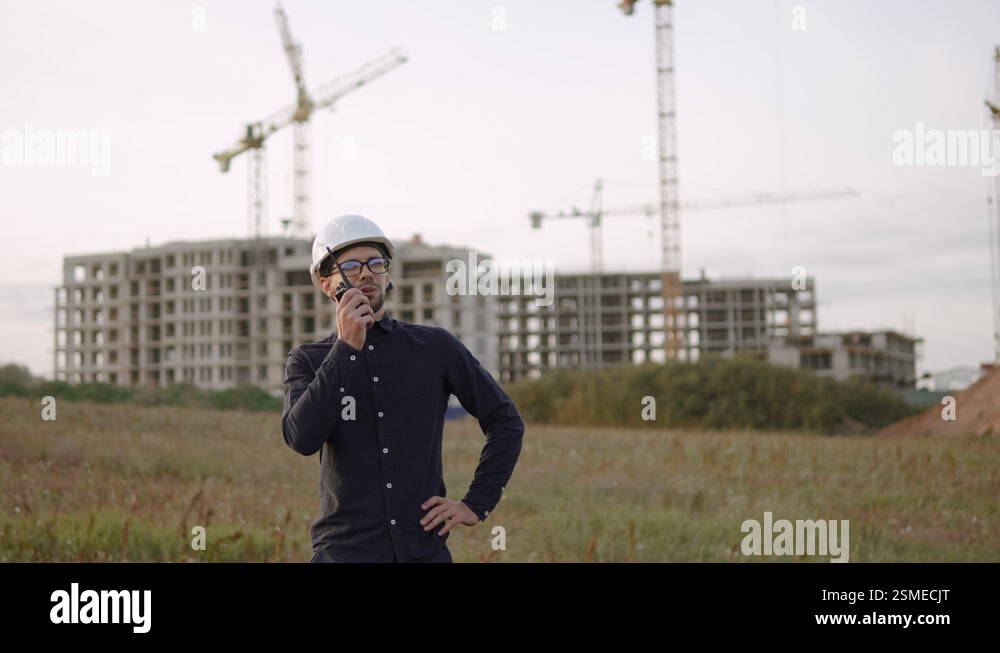 Serious man engineer walks and talks on walkie-talkie near construction ...
