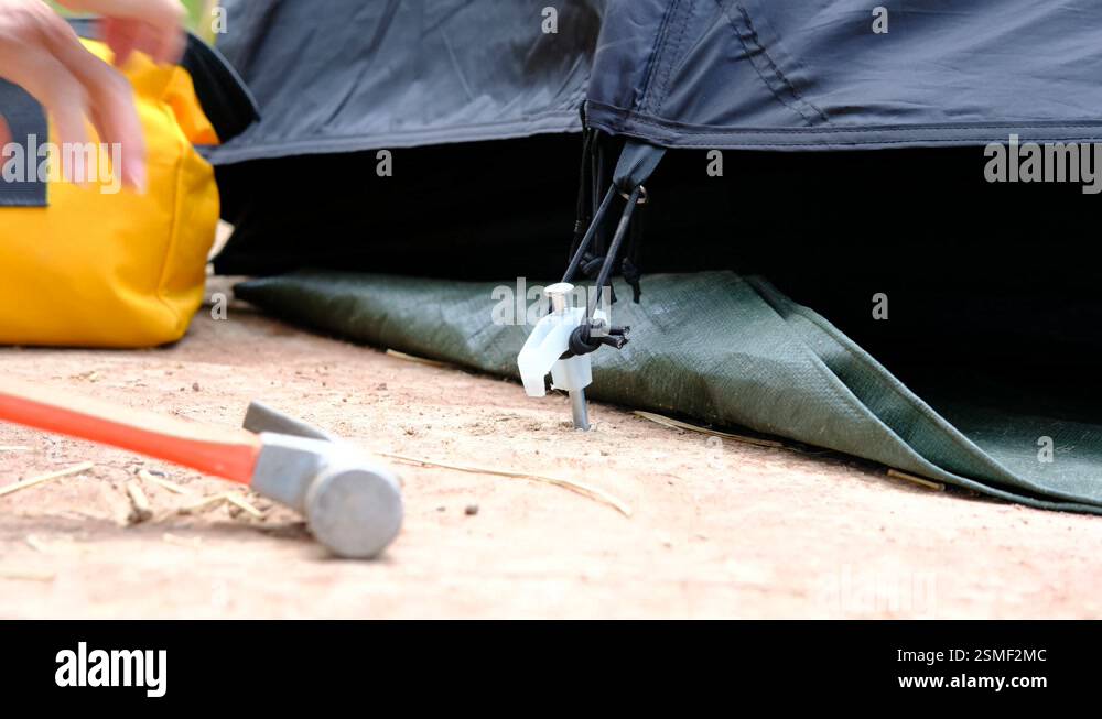 Tourists' hands use hammers to hammer into the ground to make the tents ...
