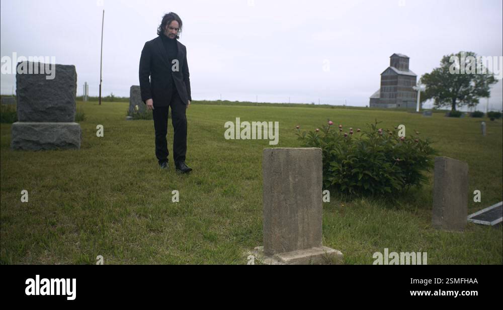 Sombre man in black suit walking past graves and tombstones in cemetery ...