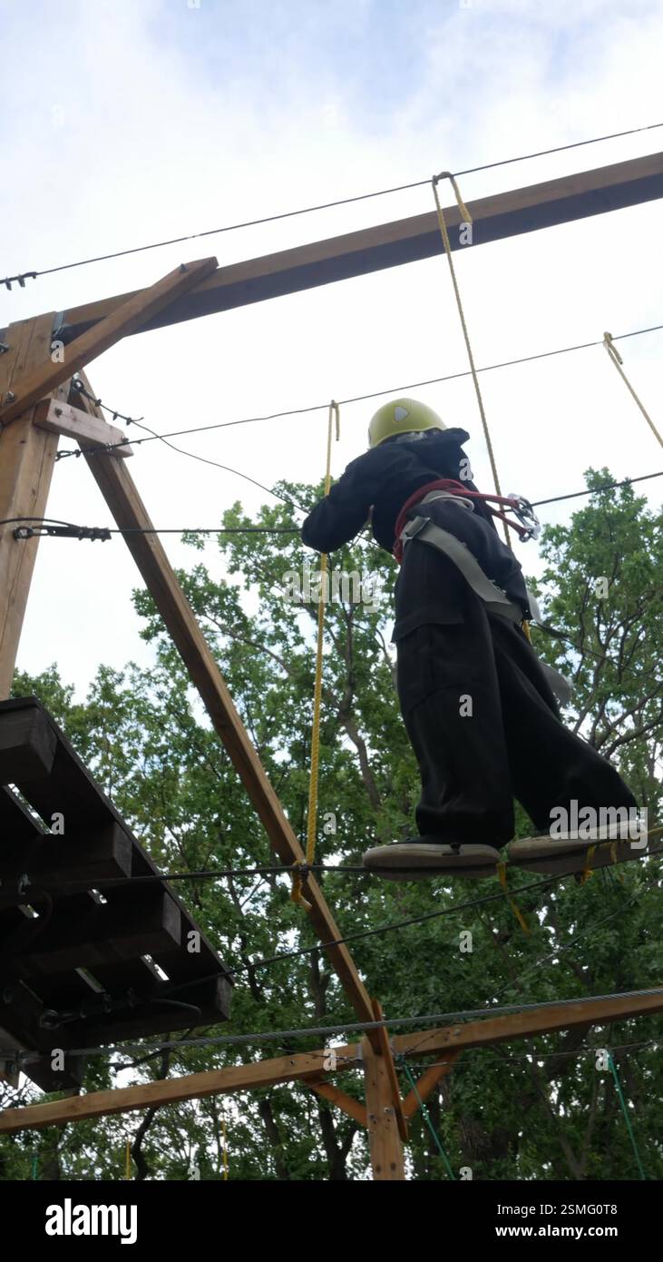 Rope park. A girl teenager in a helmet walks on suspended rope ladders ...