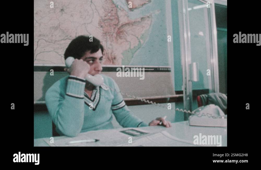 1970s: Man talks on phone near wall map. Reporters meet and talk on ...