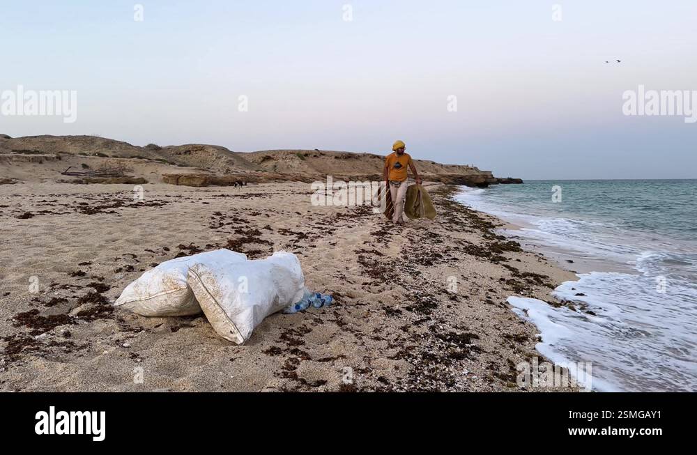 Man in orange t-shirt carrying beach garbage and two big trash bags on ...