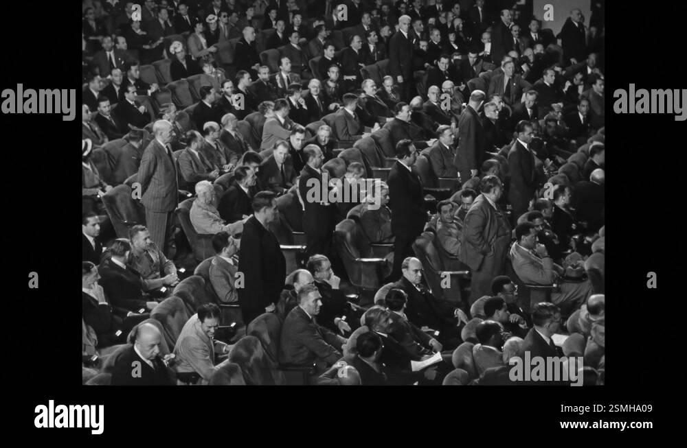 1940s: A large crowd of people gather in an auditorium, likely for a ...