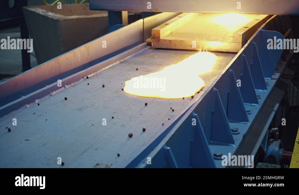 Hot liquid metal moving on a conveyor belt at industrial metallurgical ...