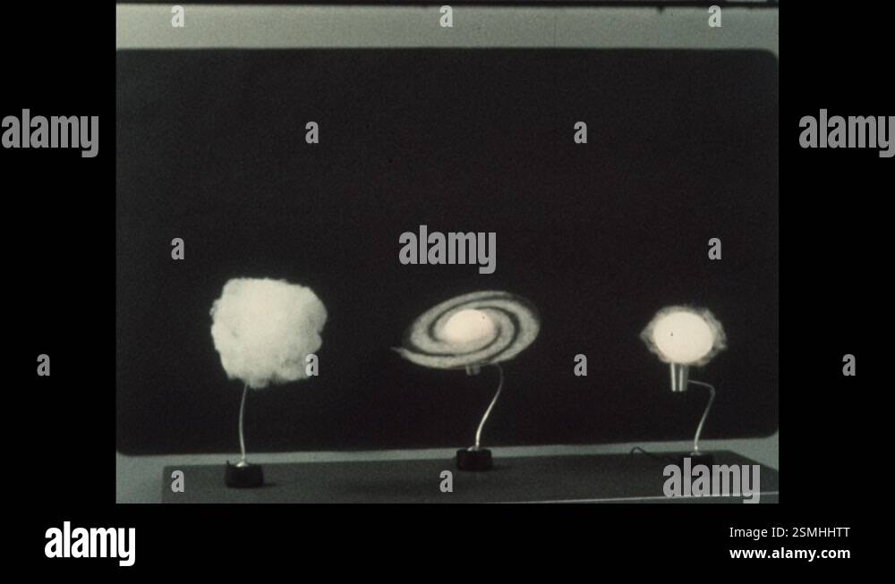 1960s: Models of nebula, solar system and star on desk. Man adjusts ...