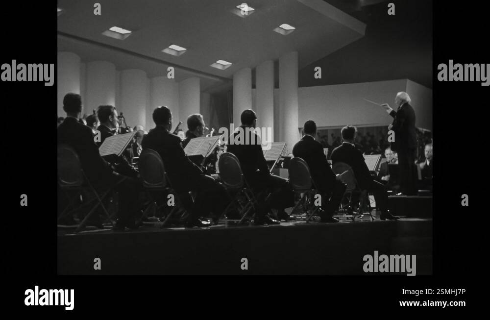 1940s: An orchestra performs on stage with a conductor directing them ...