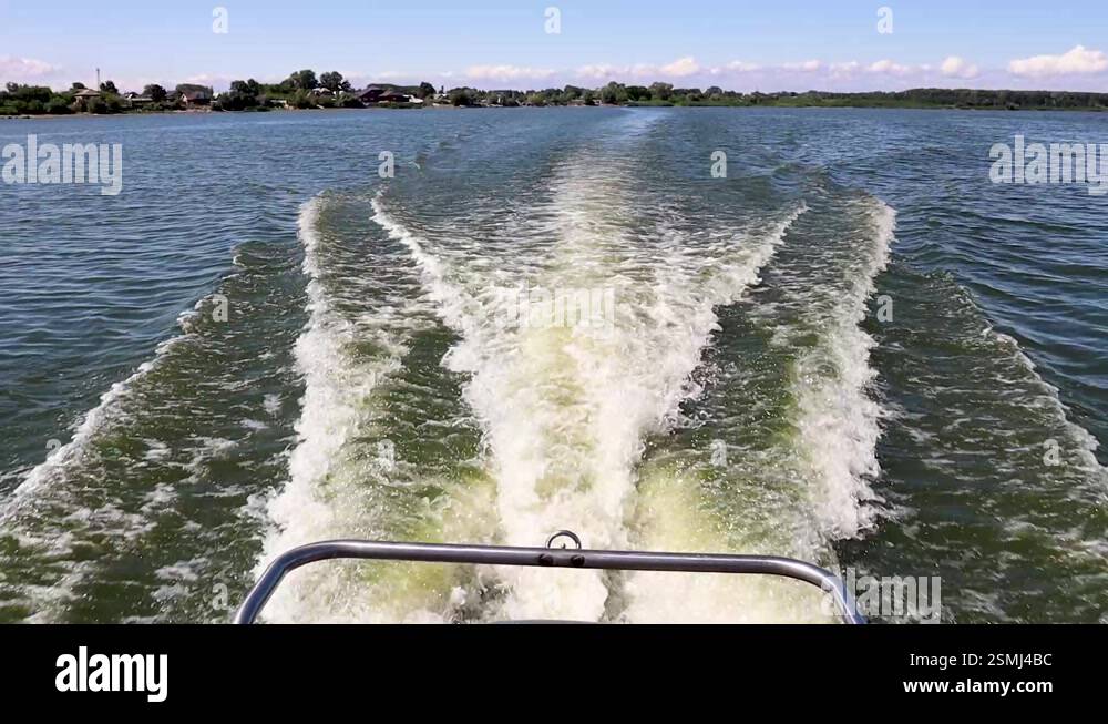 Boat glides through a river, leaving a wake of white foam in its path ...