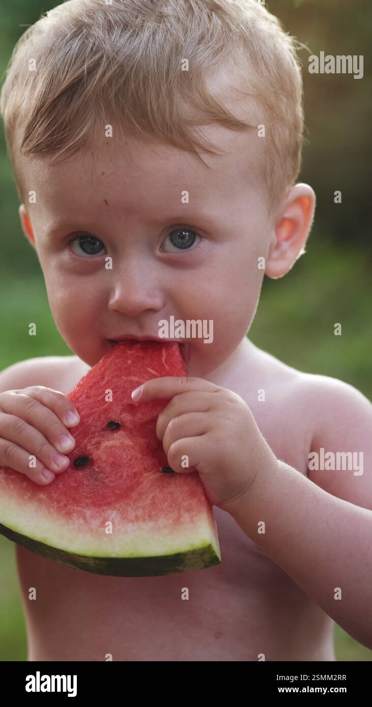 Vertical footage of funny baby kid eating watermelon outdoors in summer ...