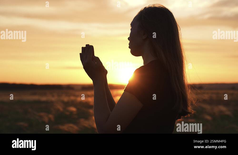 Woman praying with folded hands at sunset silhouette. Faithful girl ...