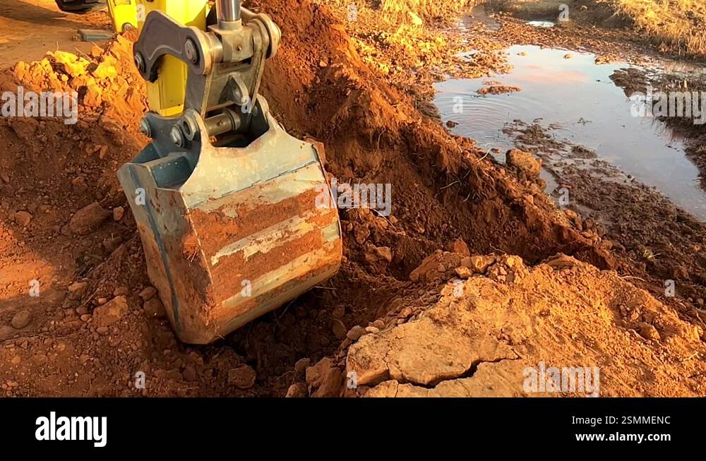 Excavator digging a trench in red iron-rich earth on sandy bank to ...