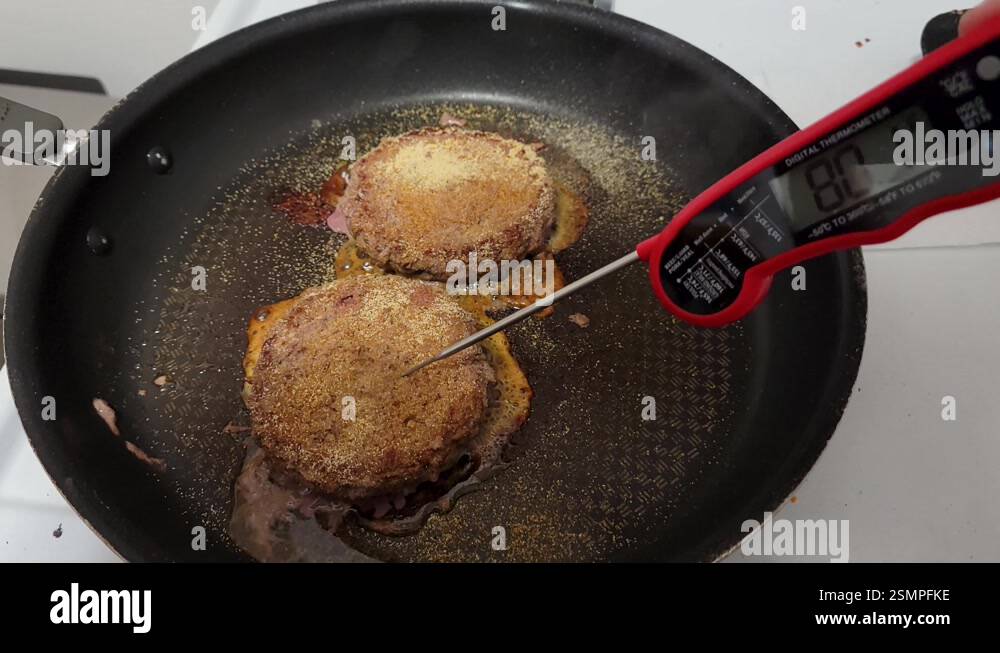 Burgers frying in a pan as a meat thermometer checks the internal Stock ...