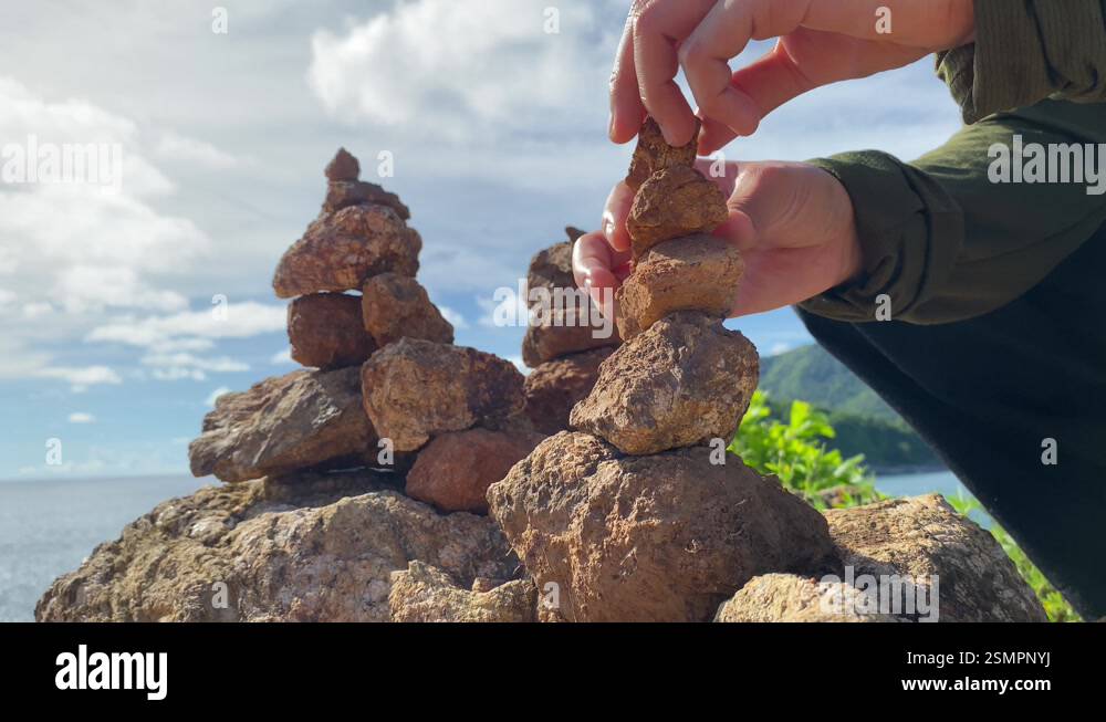 Hands stacking brown pebble rock stone on top of others on top of ...
